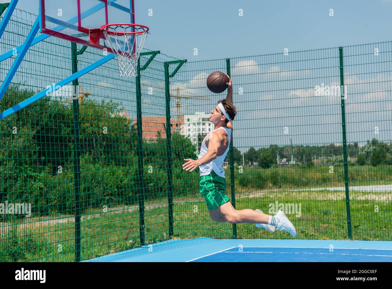 Side view of sportsman jumping under hoop while playing streetball ...
