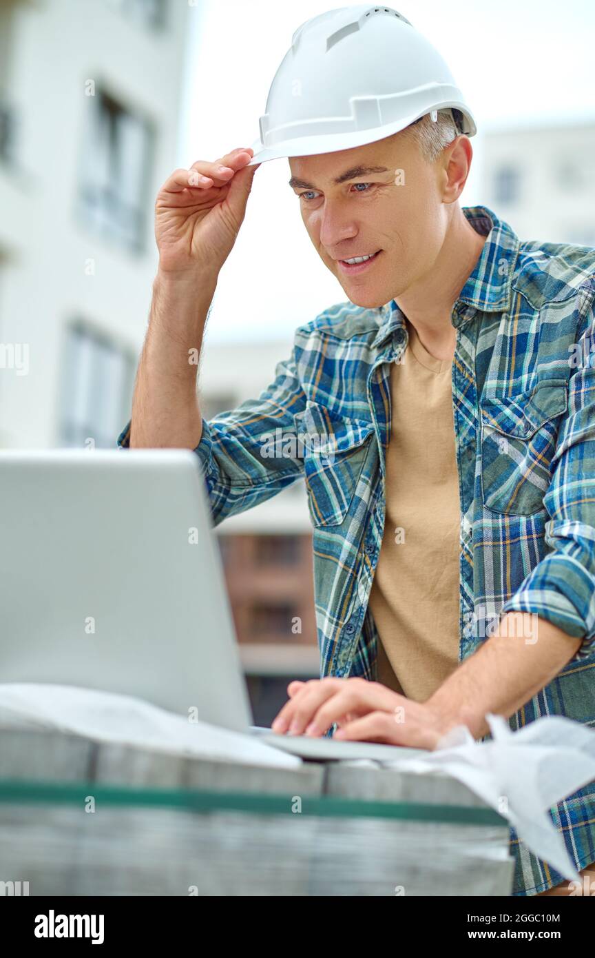 Concentrated constructor in a hardhat working on his computer outdoors ...