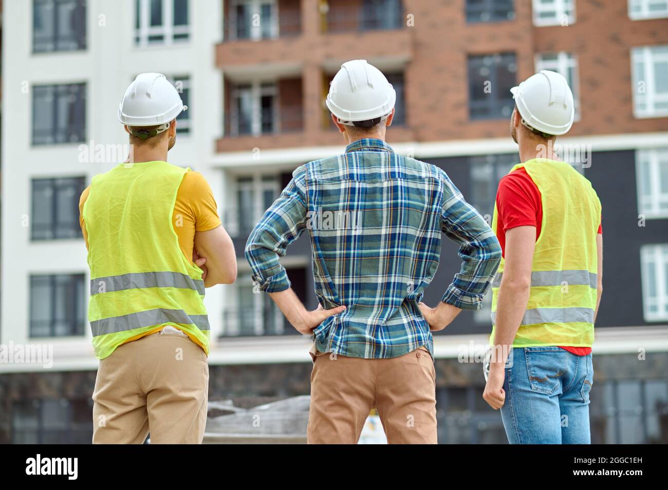 Three workers in hardhats standing before a new building Stock Photo ...