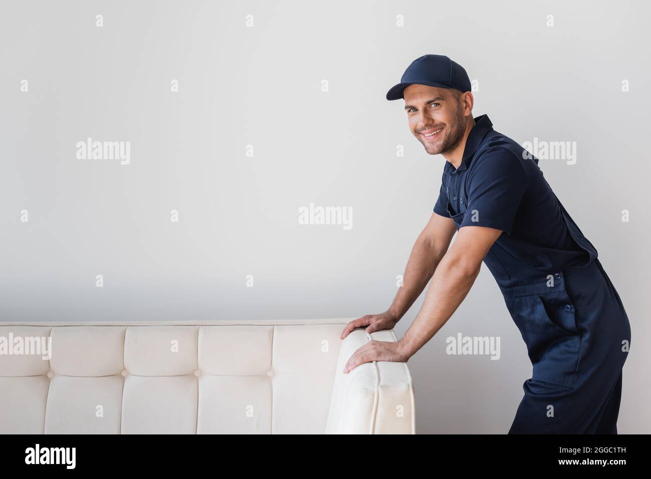 happy workman standing near white couch and smiling at camera Stock ...