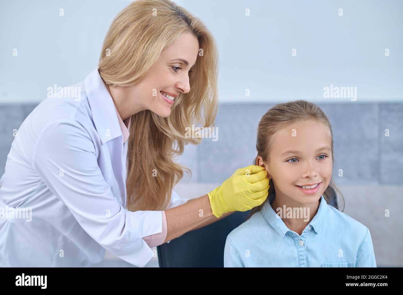 Professional audiologist putting a hearing device into the girls ear ...