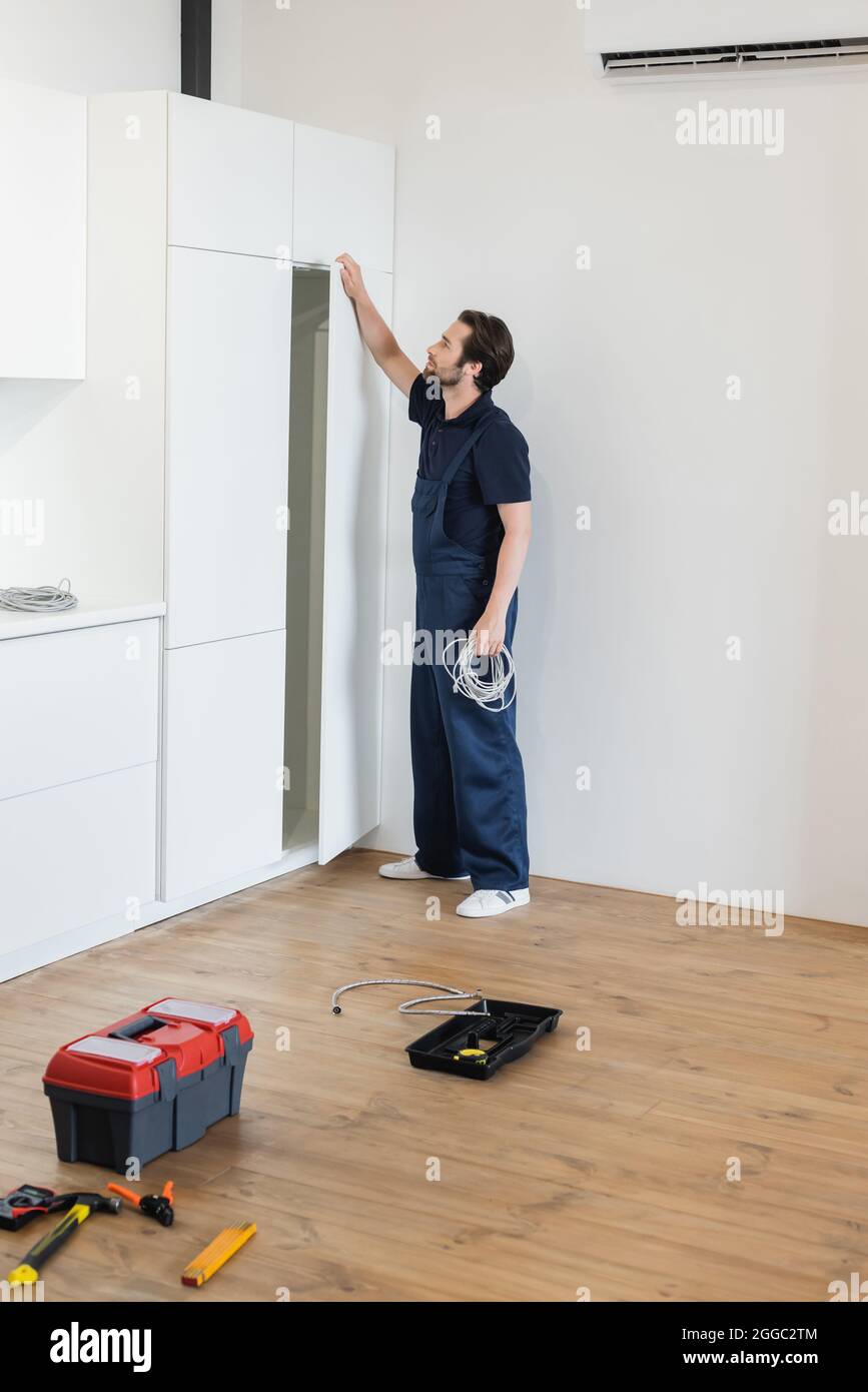 workman opening kitchen cabinet while holding cable near tools and ...