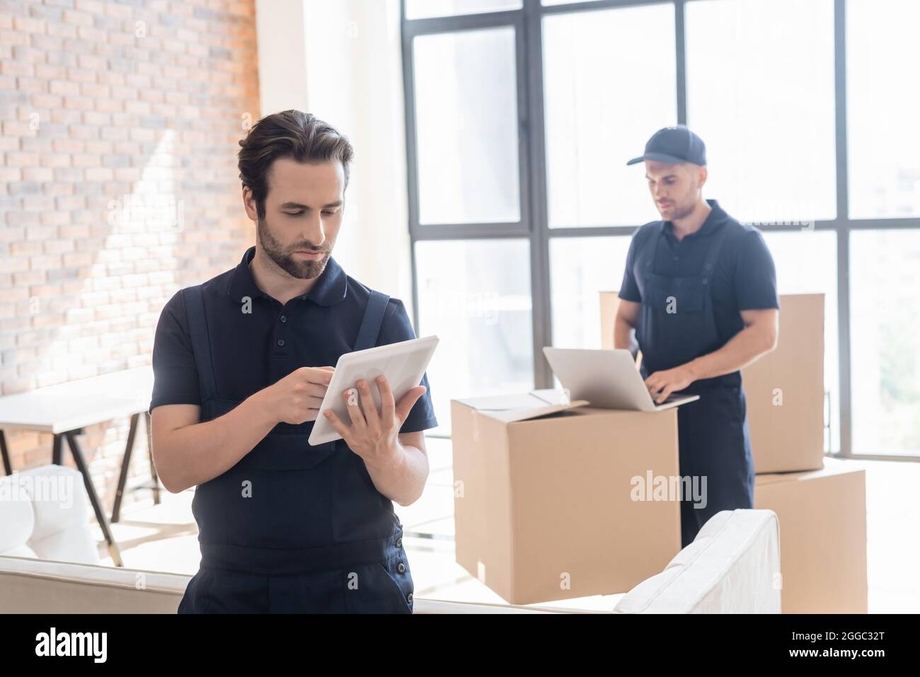 workman using digital tablet near carton boxes and blurred colleague ...