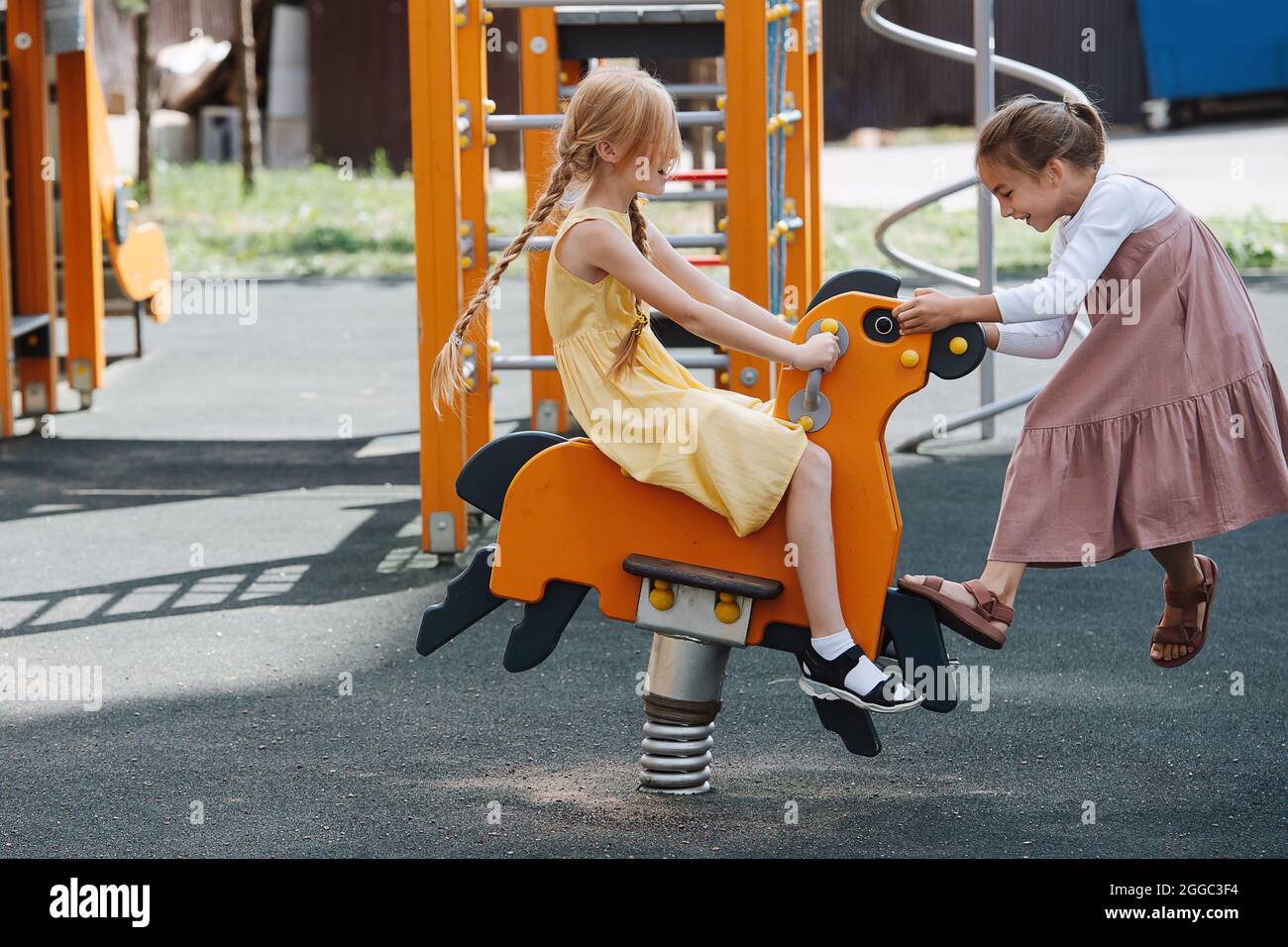 Two happy little girls playing with a spring horse on a children ...