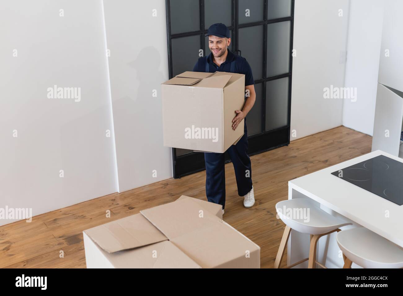 smiling mover carrying cardboard box in apartment Stock Photo - Alamy