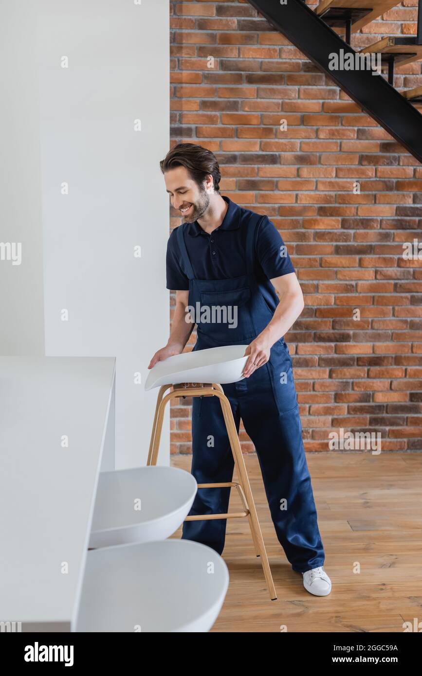 smiling man holding stool near white table in kitchen Stock Photo - Alamy