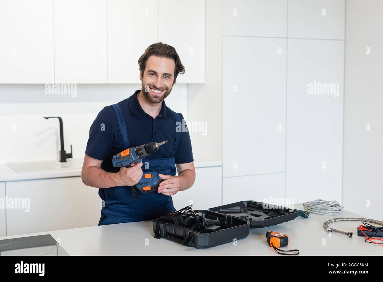 happy workman with electric drill looking at camera near tools on ...
