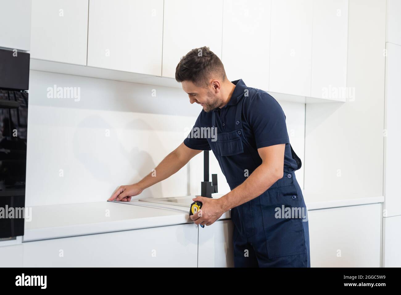 man in overalls measuring tabletop of white furniture in kitchen Stock ...