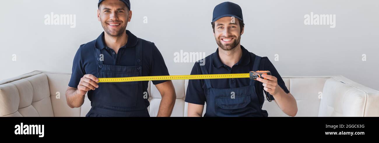 happy movers holding measuring tape while sitting on couch, banner ...