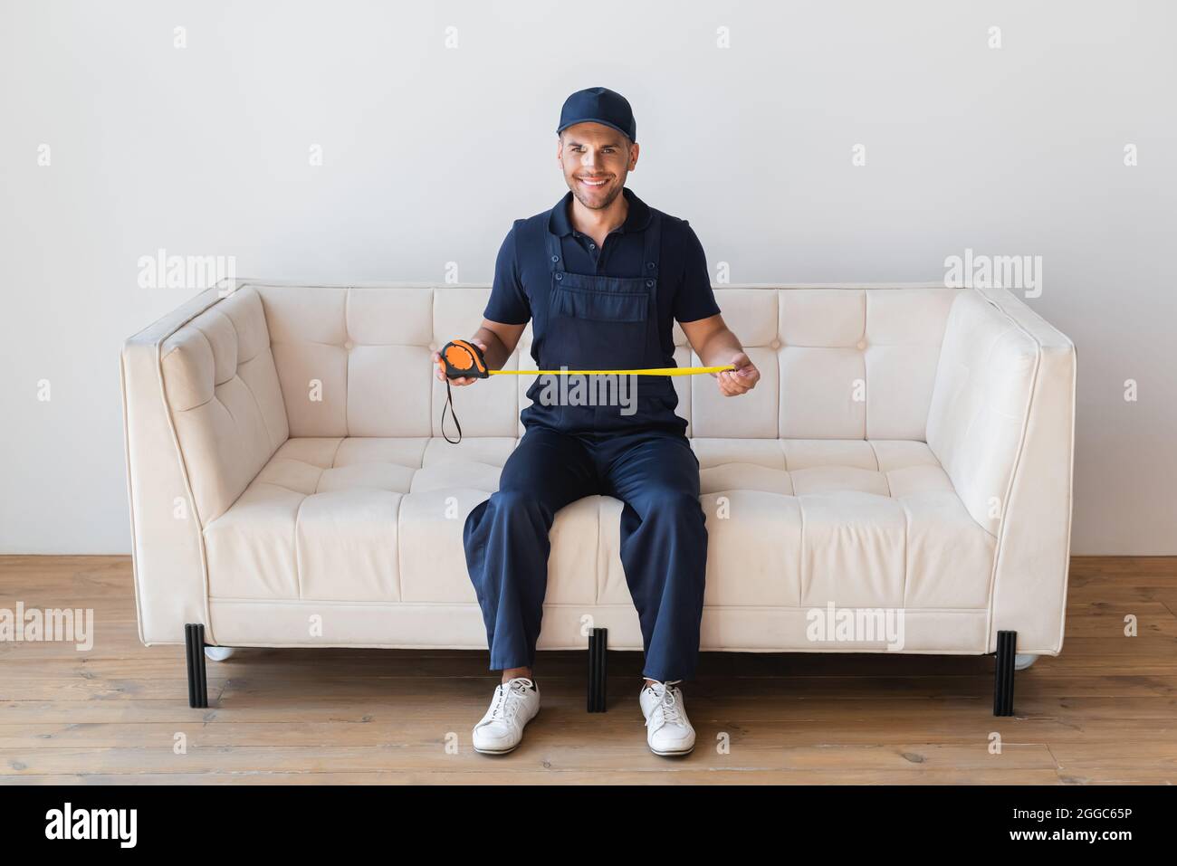 full length view of smiling handyman sitting on white couch with ...