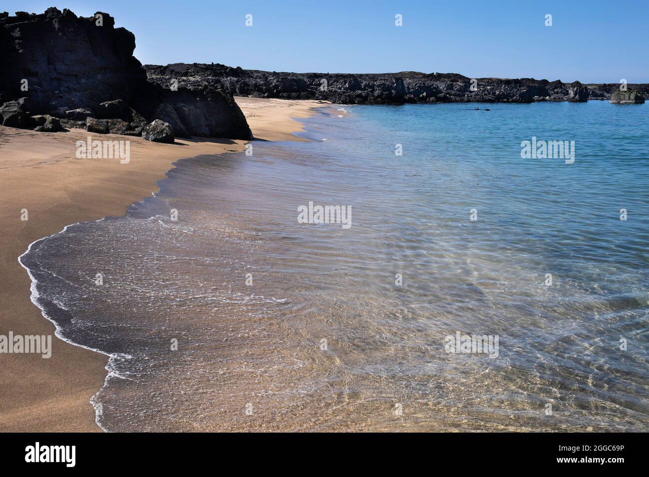 Empty sandy beach with crystal clear water and black lava stones and ...