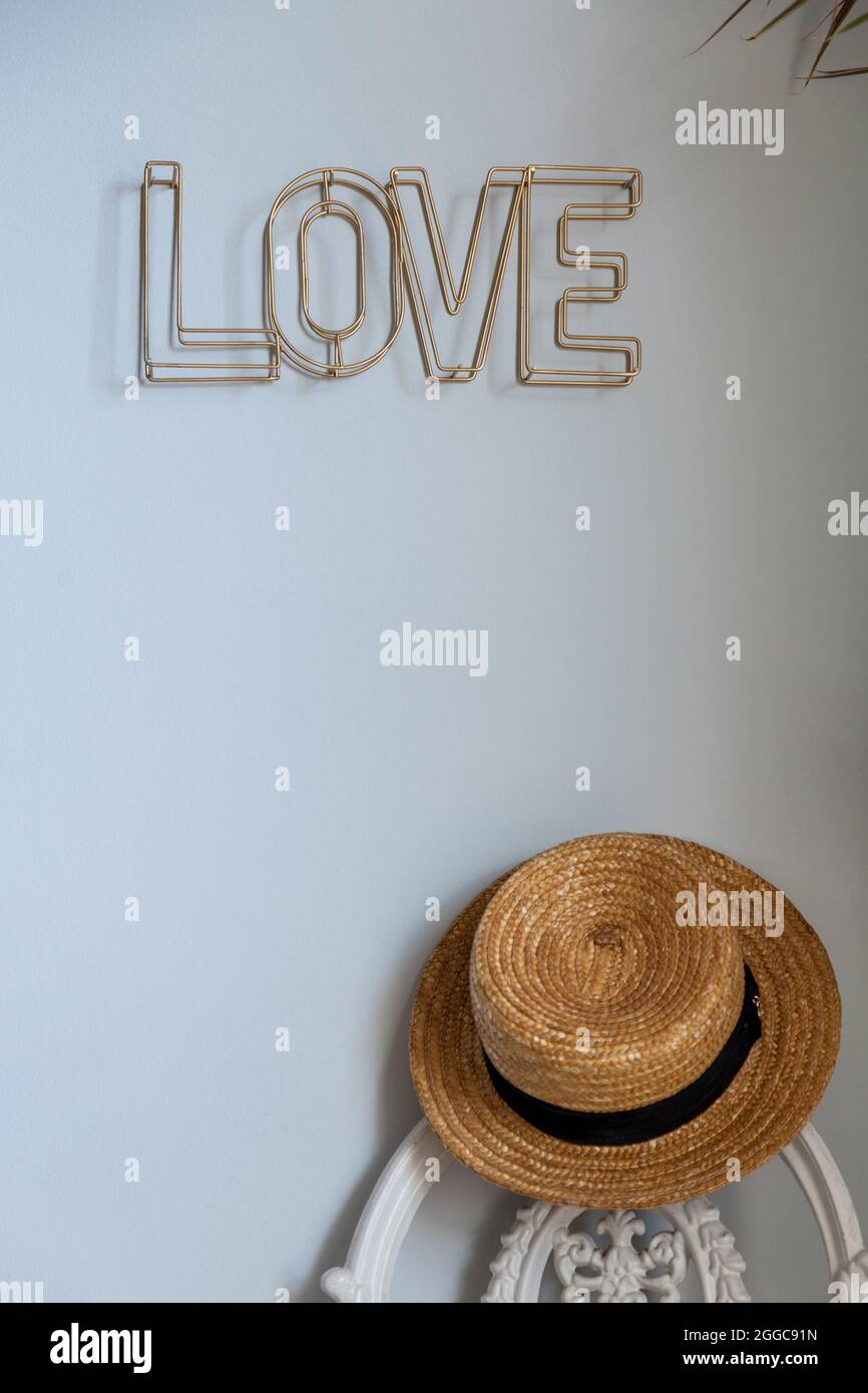 Vertical shot of straw hat hanging on chair back leaned on the wall and ...