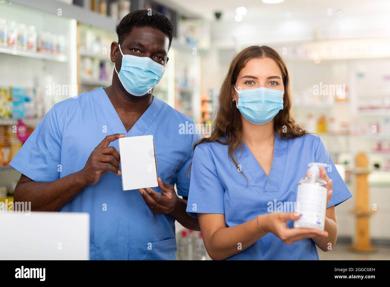 Portrait of two pharmacists in protective masks, demonstrating goods in ...