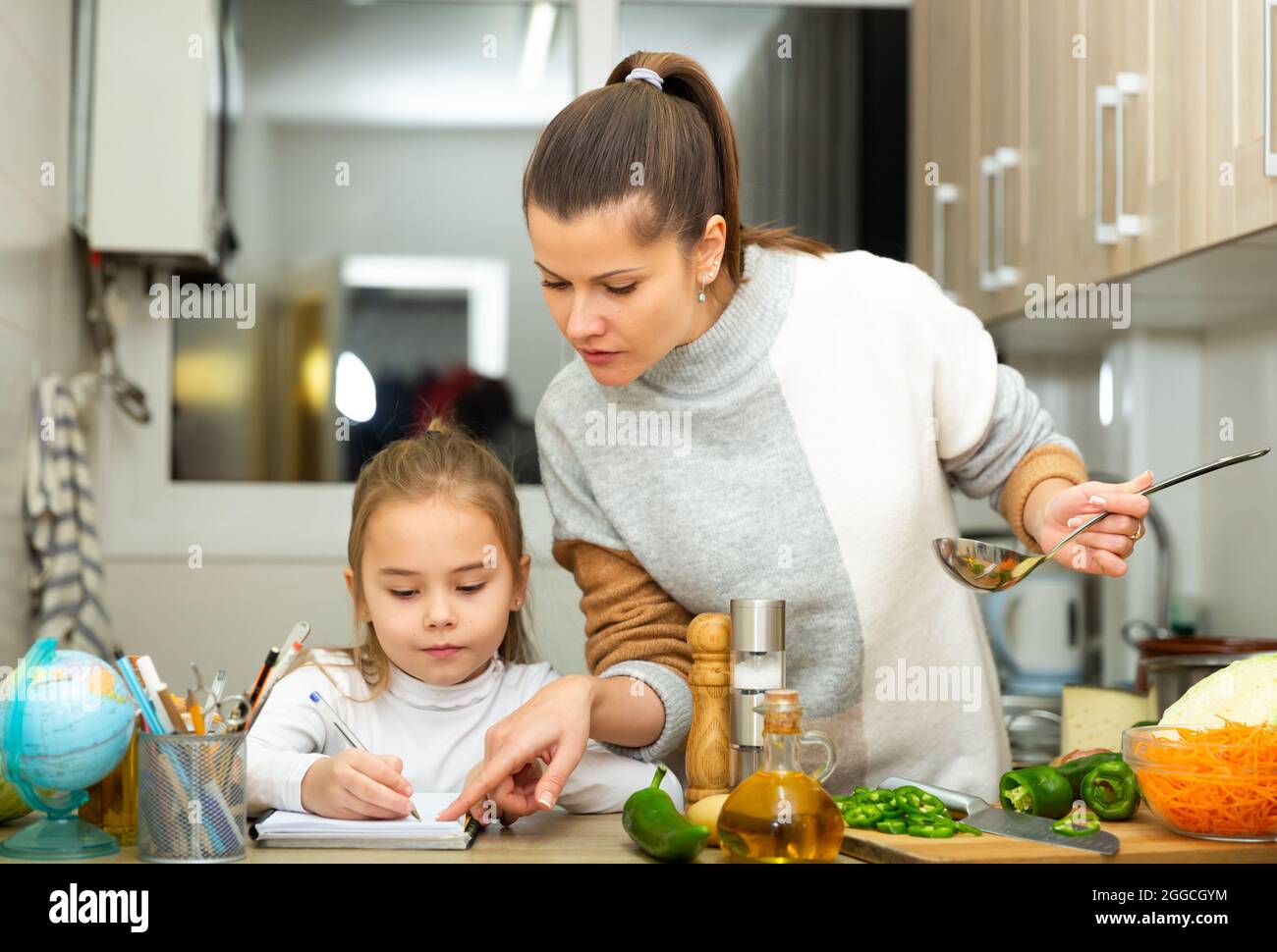Mother cooking and little daughter doing school homework Stock Photo ...