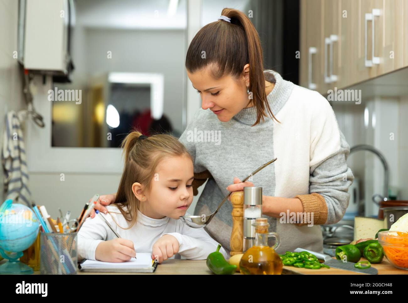 Girl writing school lesson during mother cooking at kitchen Stock Photo ...