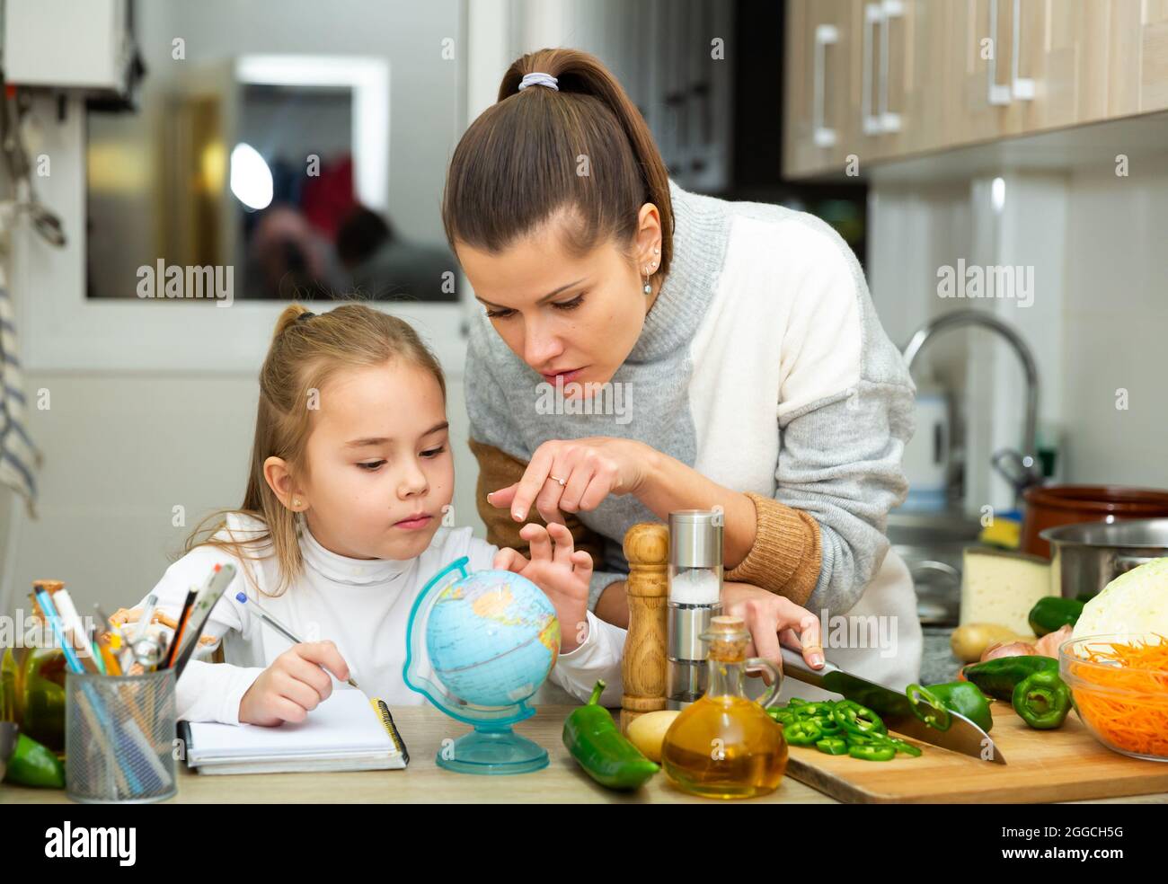 Mother cooking and little daughter doing school homework Stock Photo ...