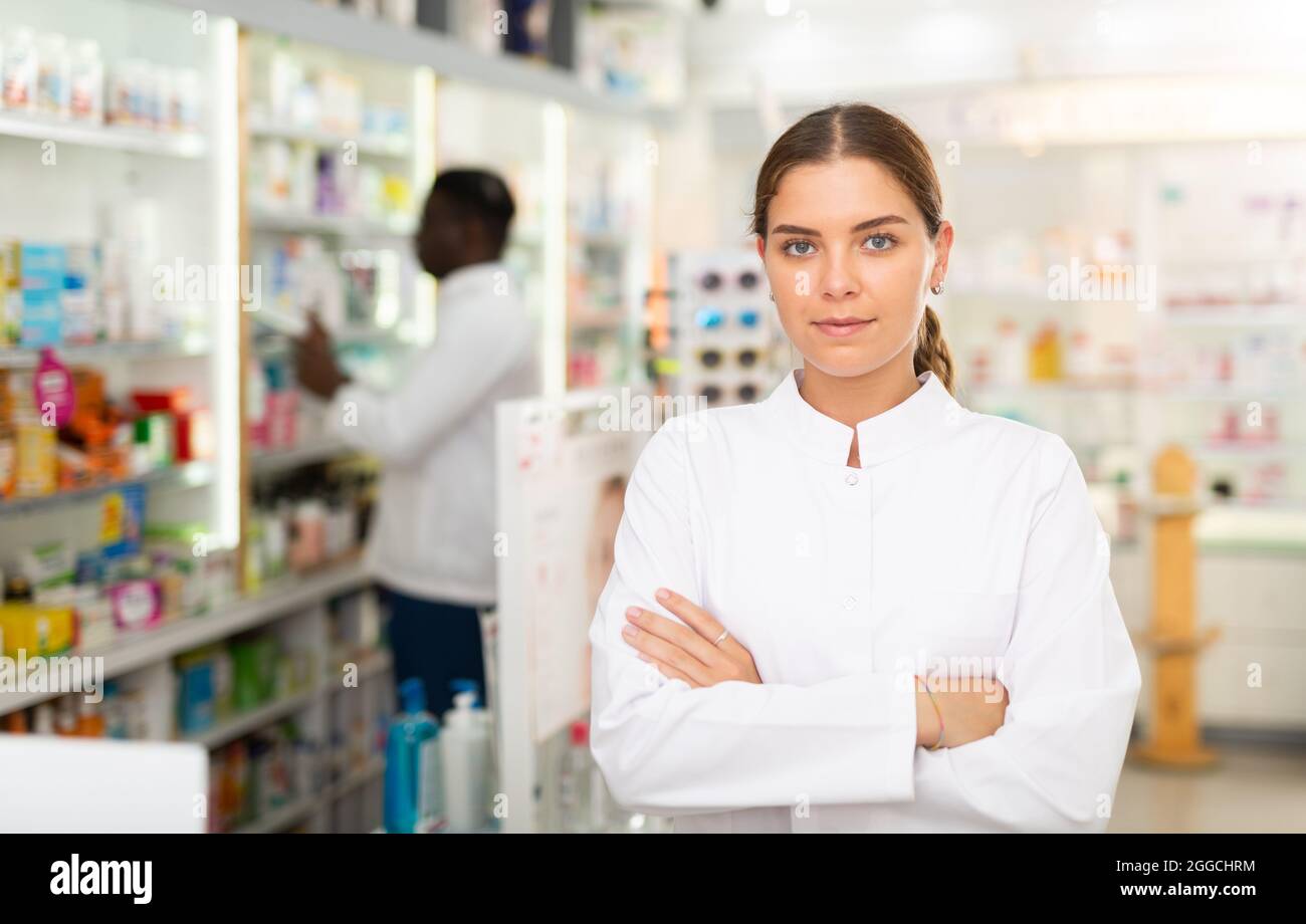 Portrait of a positive young female pharmacist in a pharmacy, standing ...
