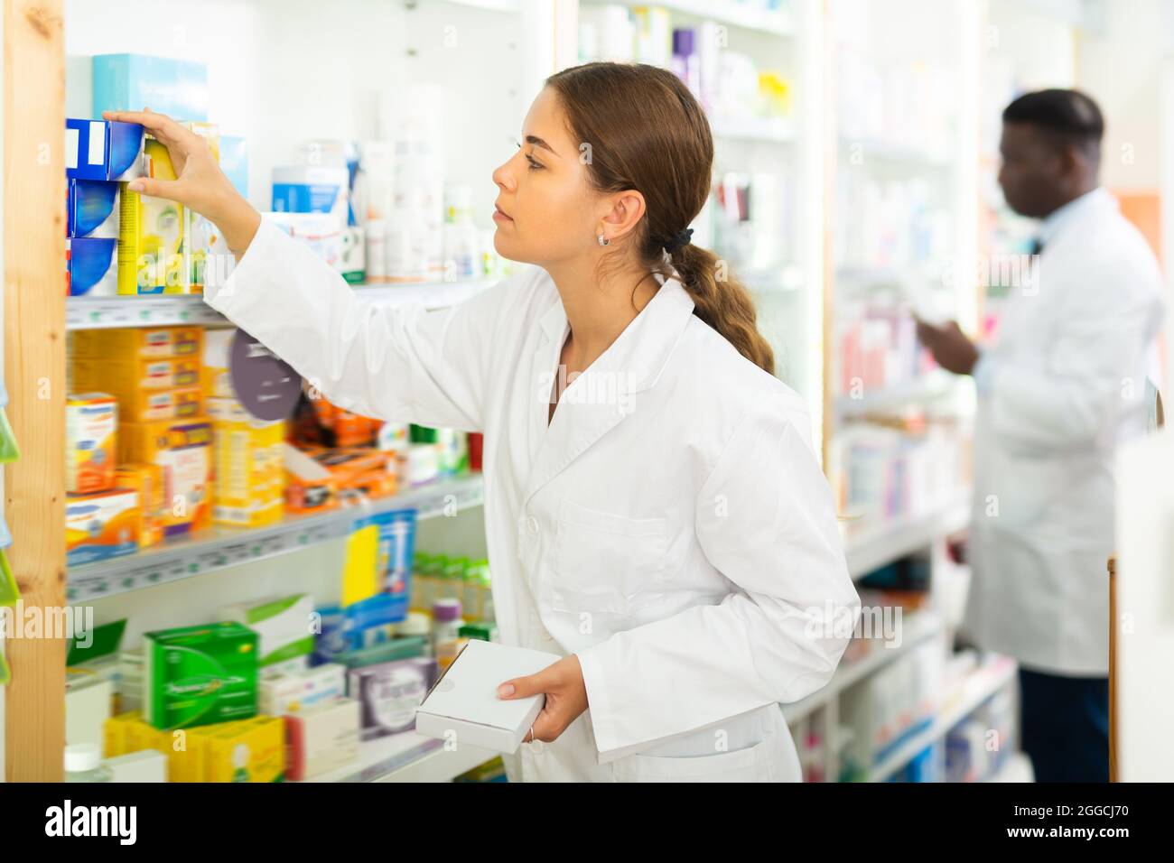 Portrait of a young female pharmacist laying out goods on the shelves ...