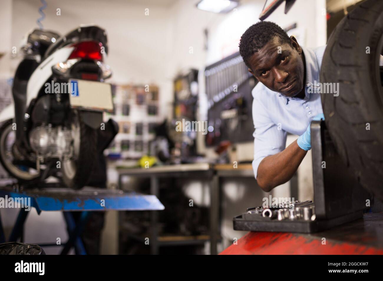 Afro american worker inspects the wheel of a motorcycle Stock Photo - Alamy