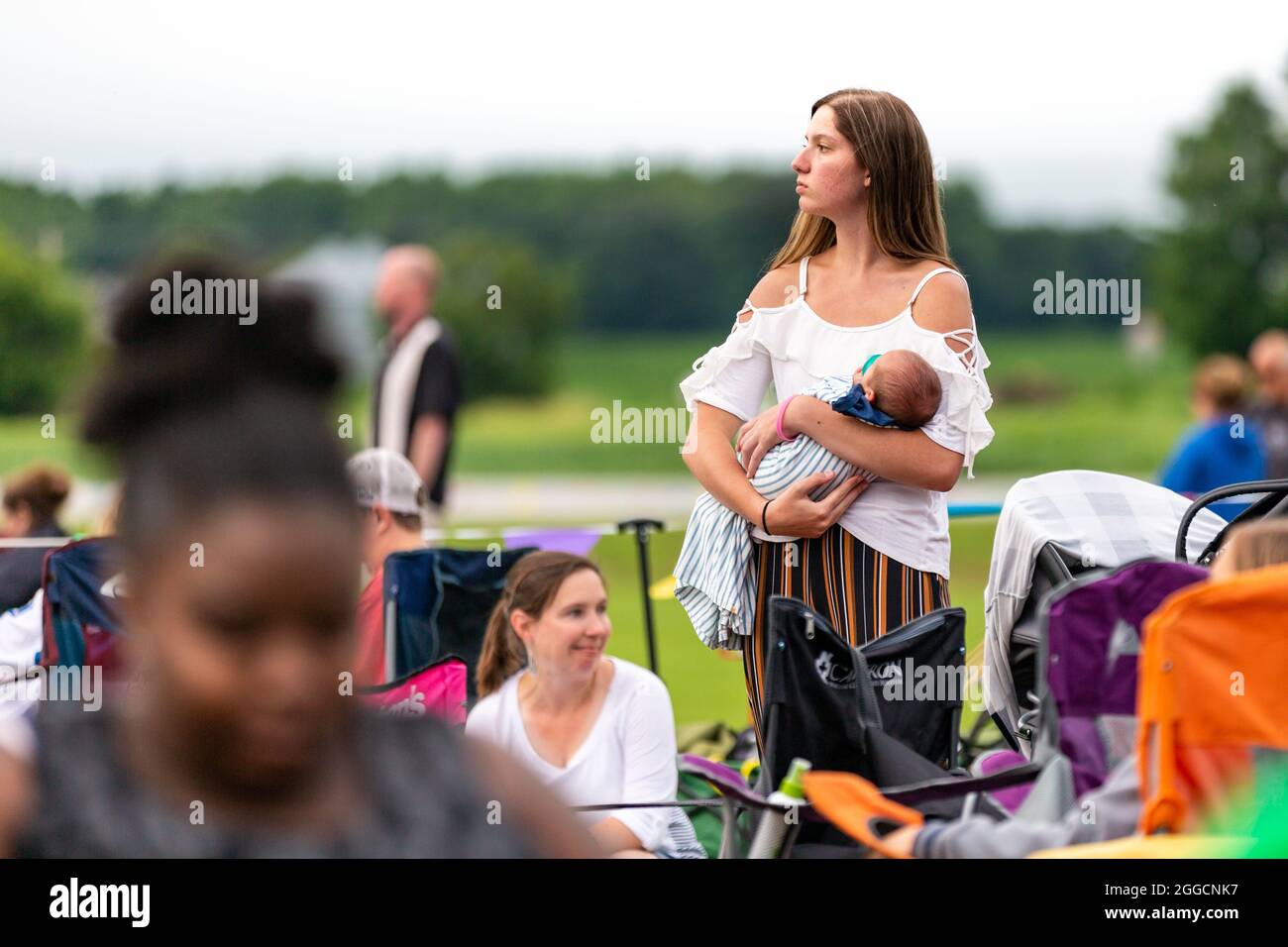 A young mother cradles her baby amidst the crowd at an outdoor concert ...