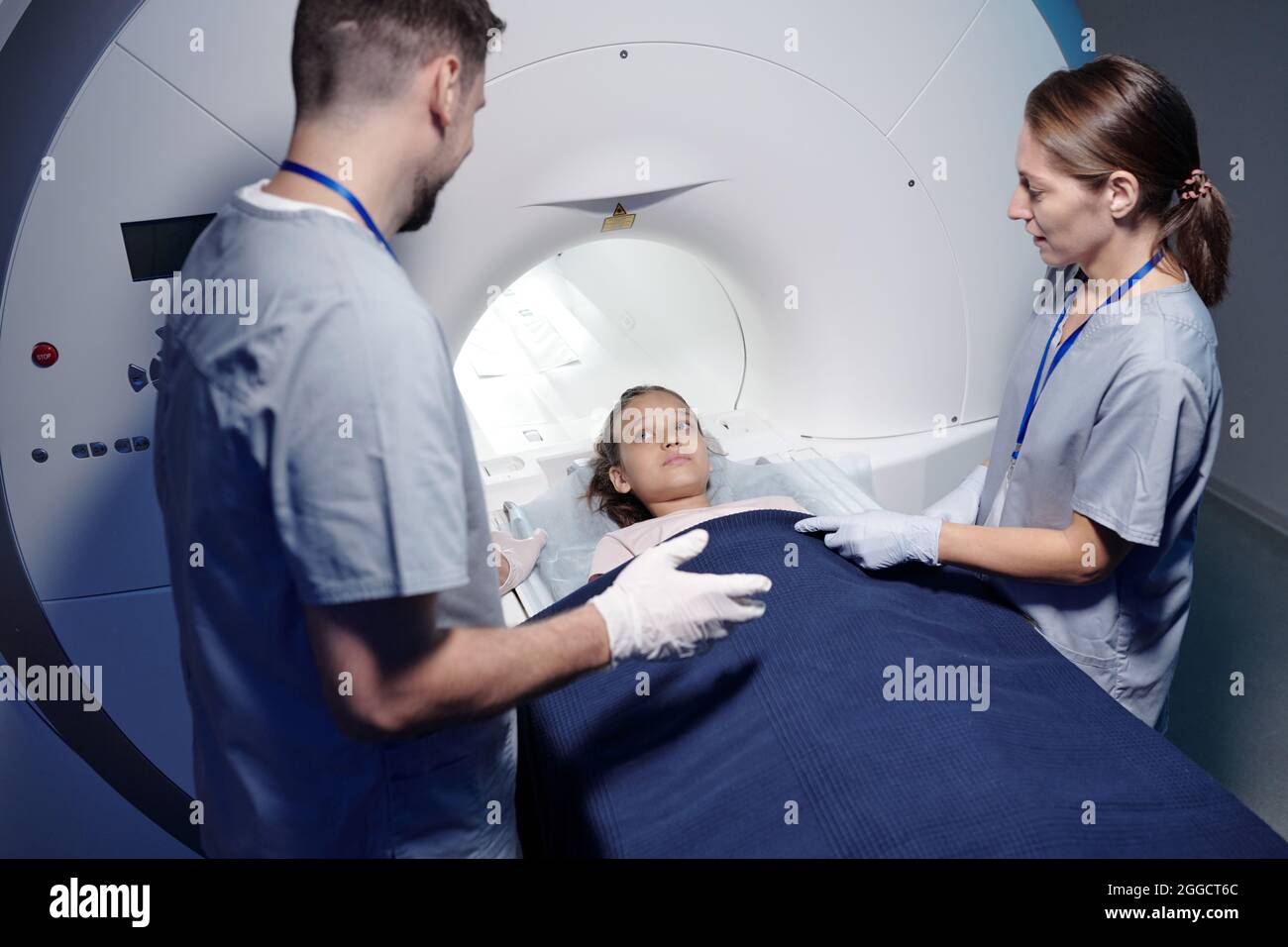 Cute little patient looking at one of radiographers while lying on ...