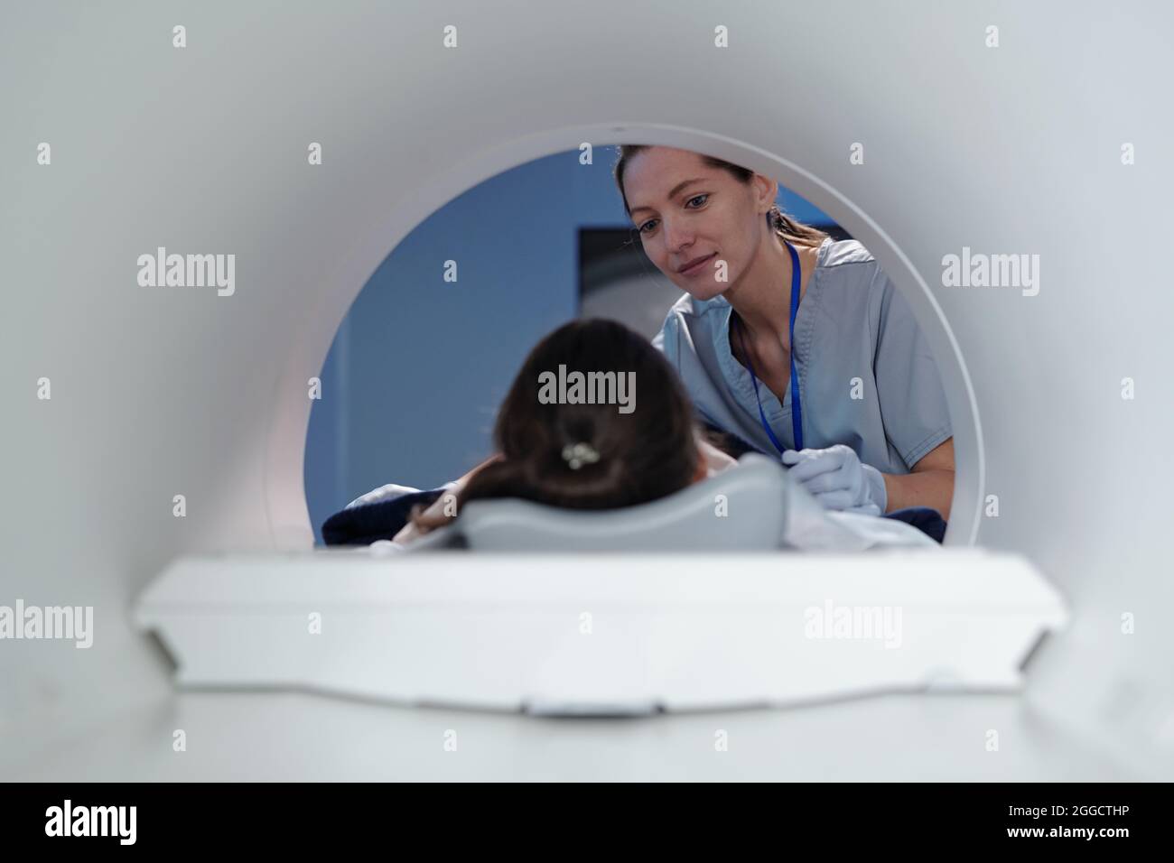 Young female clinician looking at little girl lying on table of mri ...