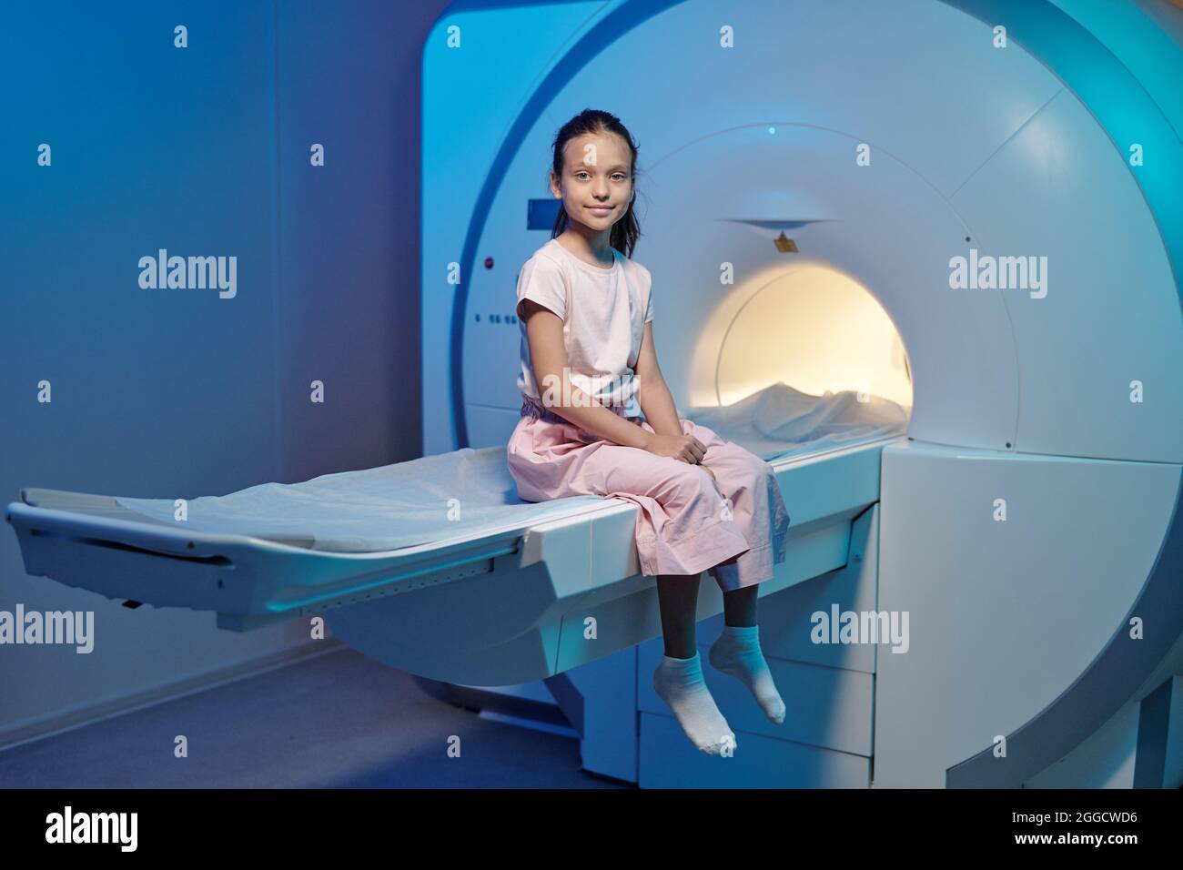 Smiling little patient sitting on long medical table before or after ...