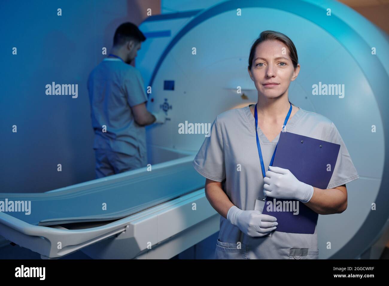 Young nurse in uniform and gloves standing in front of medical machine ...