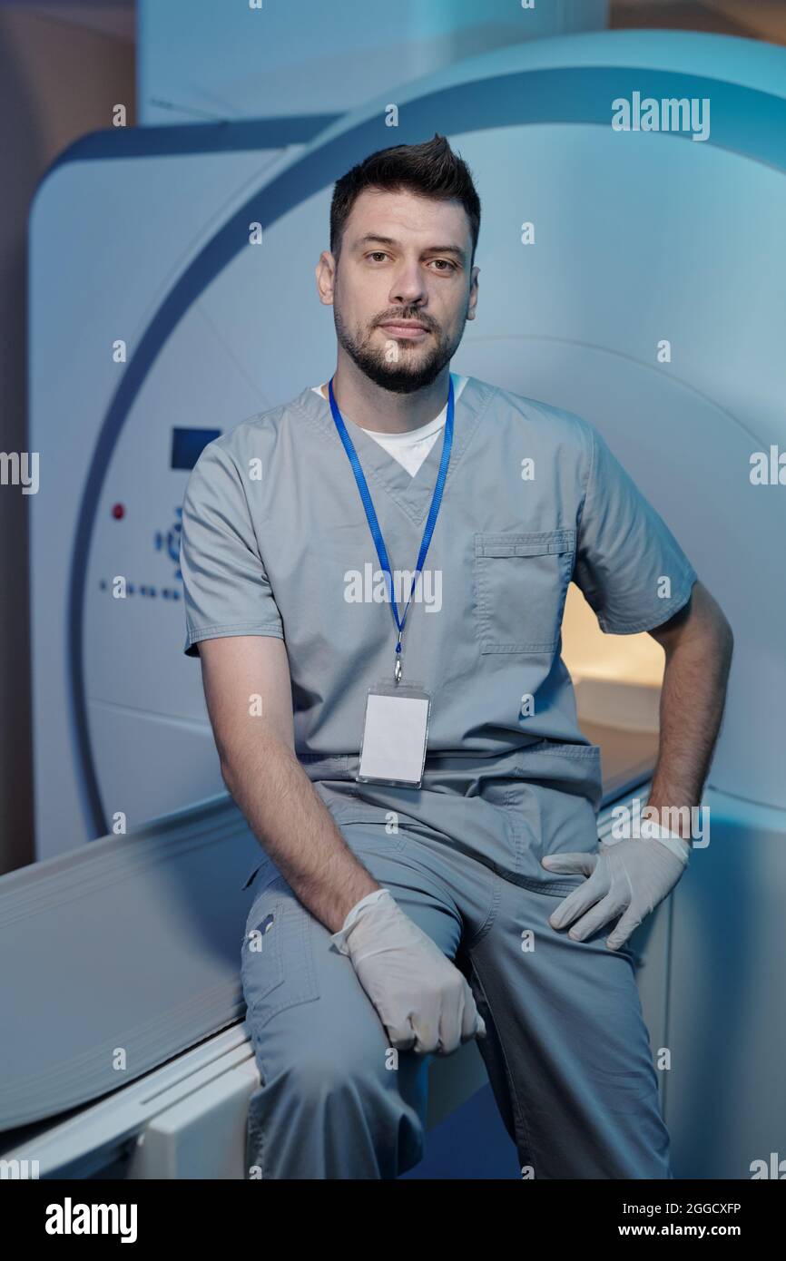 Confident worker of medical laboratory sitting on table of ct equipment ...
