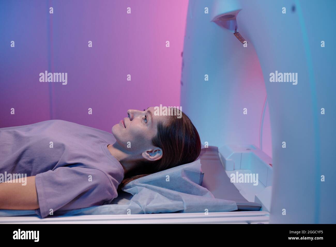 Side view of young woman lying on table of mri scan machine and waitinf ...