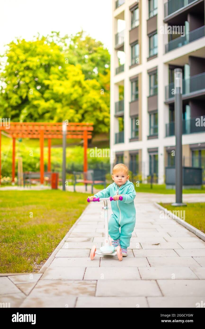 Cute little toddler girl in blue overalls riding on kick scooter. Happy ...
