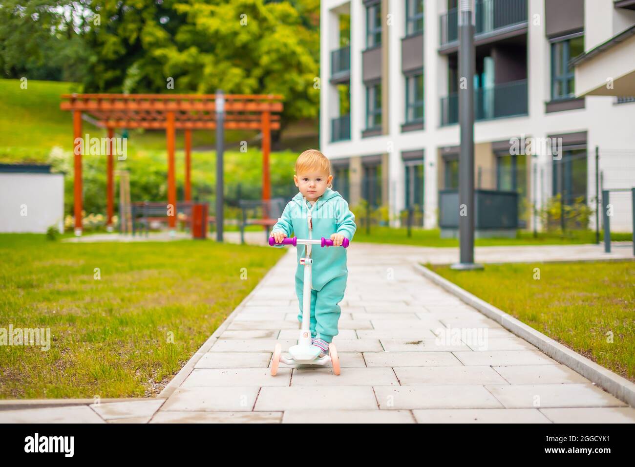 Cute little toddler girl in blue overalls riding on kick scooter. Happy ...