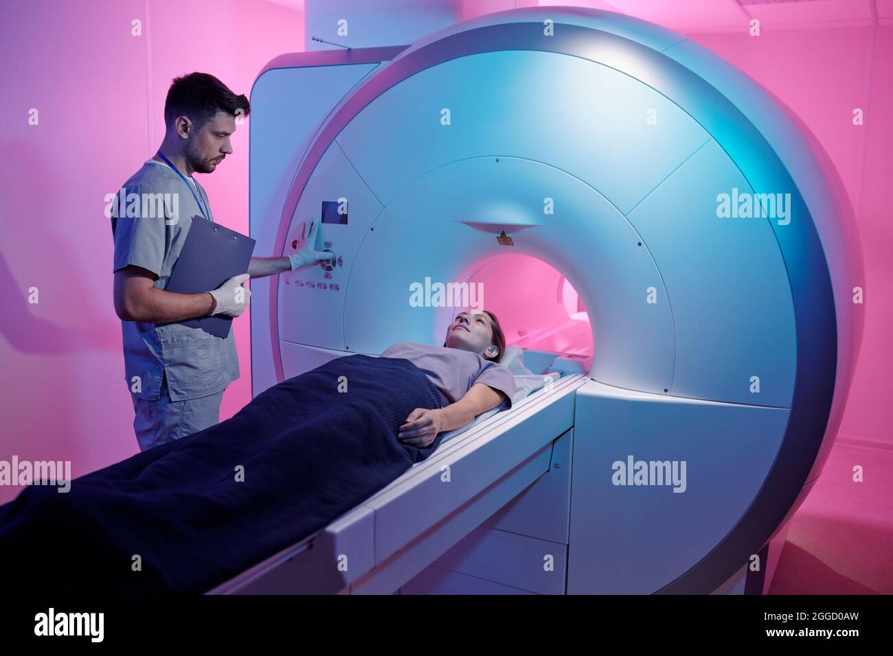 Young doctor in uniform pressing start button of mri scan machine with ...