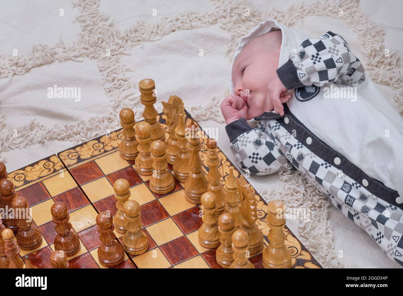 Newborn baby boy in a chess suit near a chessboard with placed pieces ...