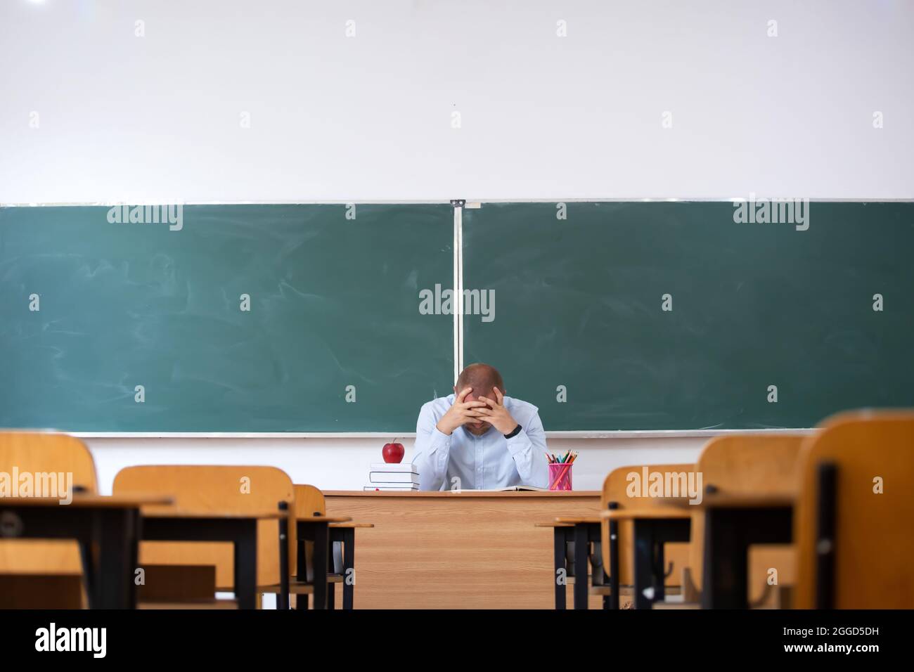 Exhausted teacher in the classroom in fron of the blackboard. Back to ...