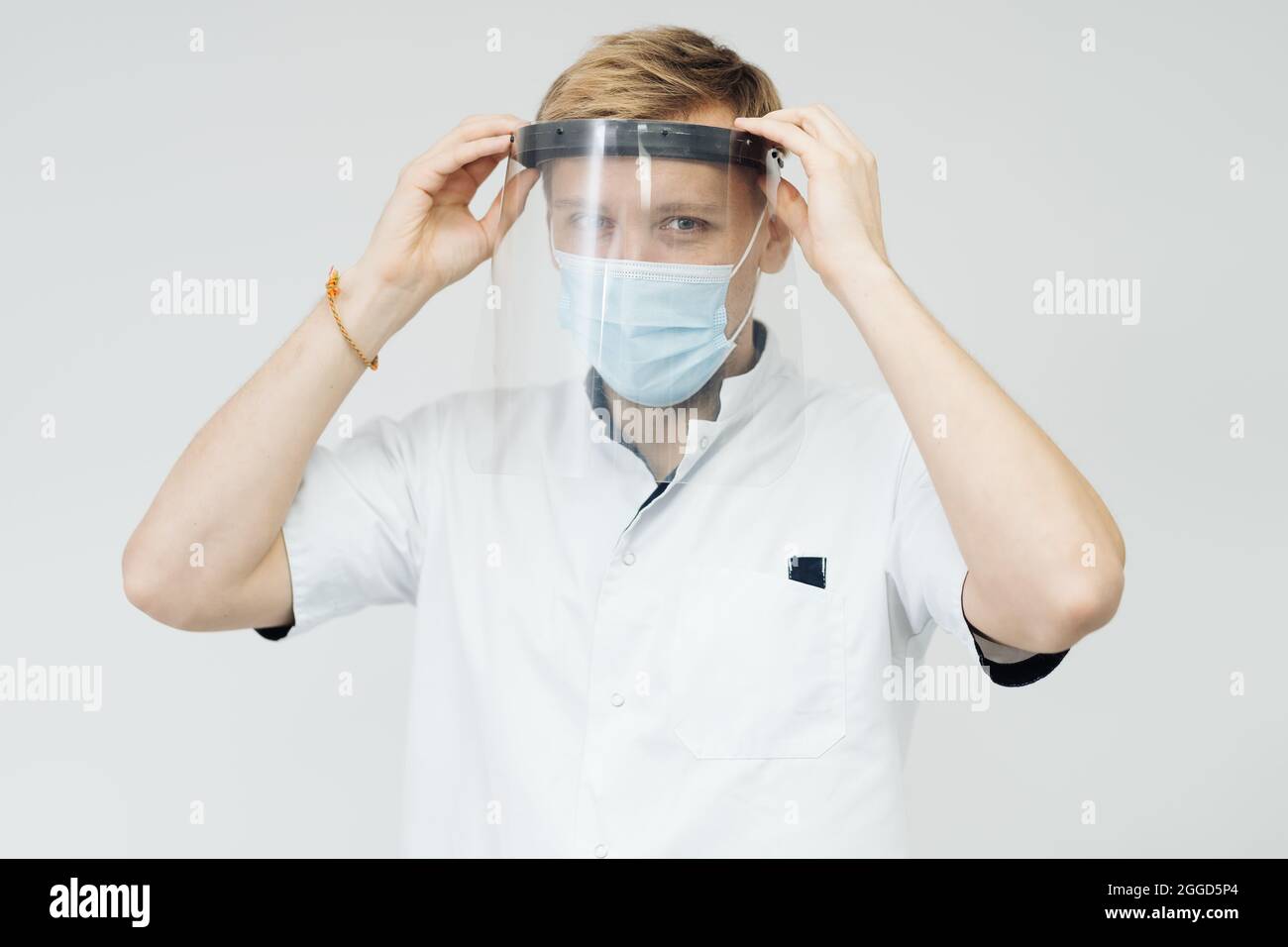Portrait of a young male medical doctor putting sterile mask isolated ...