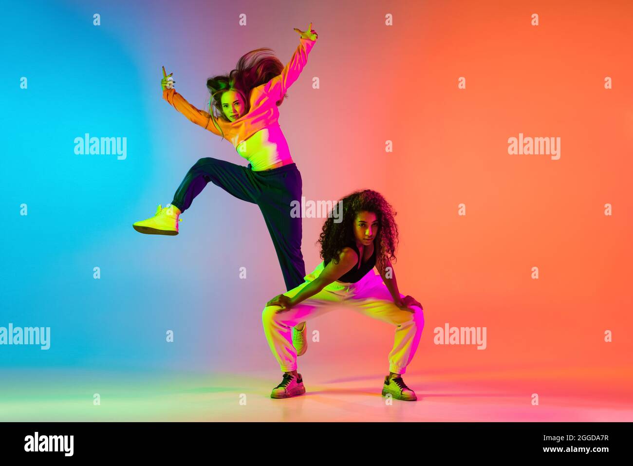 Two beautiful girls dancing hip-hop on colorful gradient background in ...