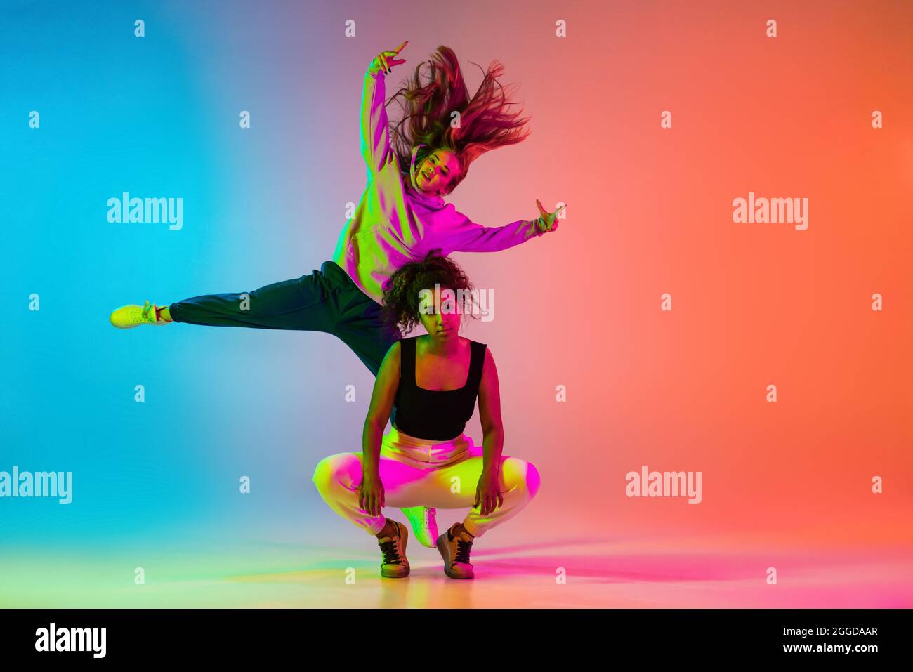 Two beautiful hip-hop girls dancing on gradient blue orange backlground ...