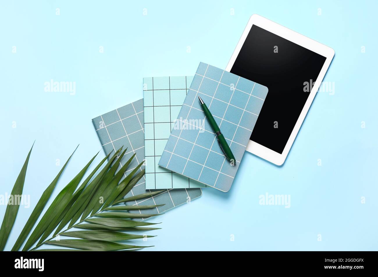 Composition with notebooks, pen, tablet computer and palm leaf on color ...