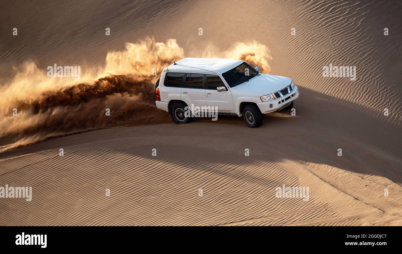 a white car or suv is going up from a sand dune and splashing sands on ...