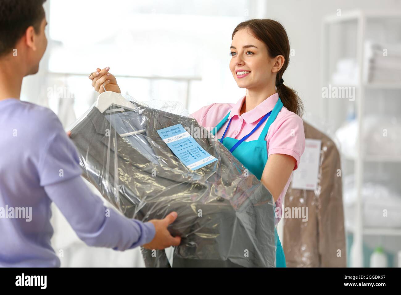 Female worker giving clean clothes to client at modern dry-cleaner's ...