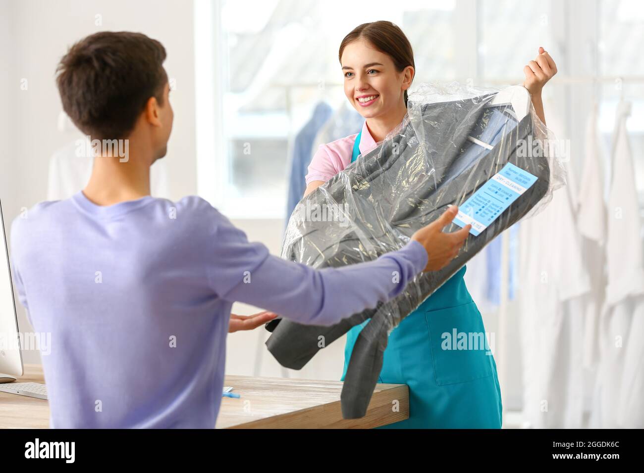 Female worker giving clean clothes to client at modern dry-cleaner's ...