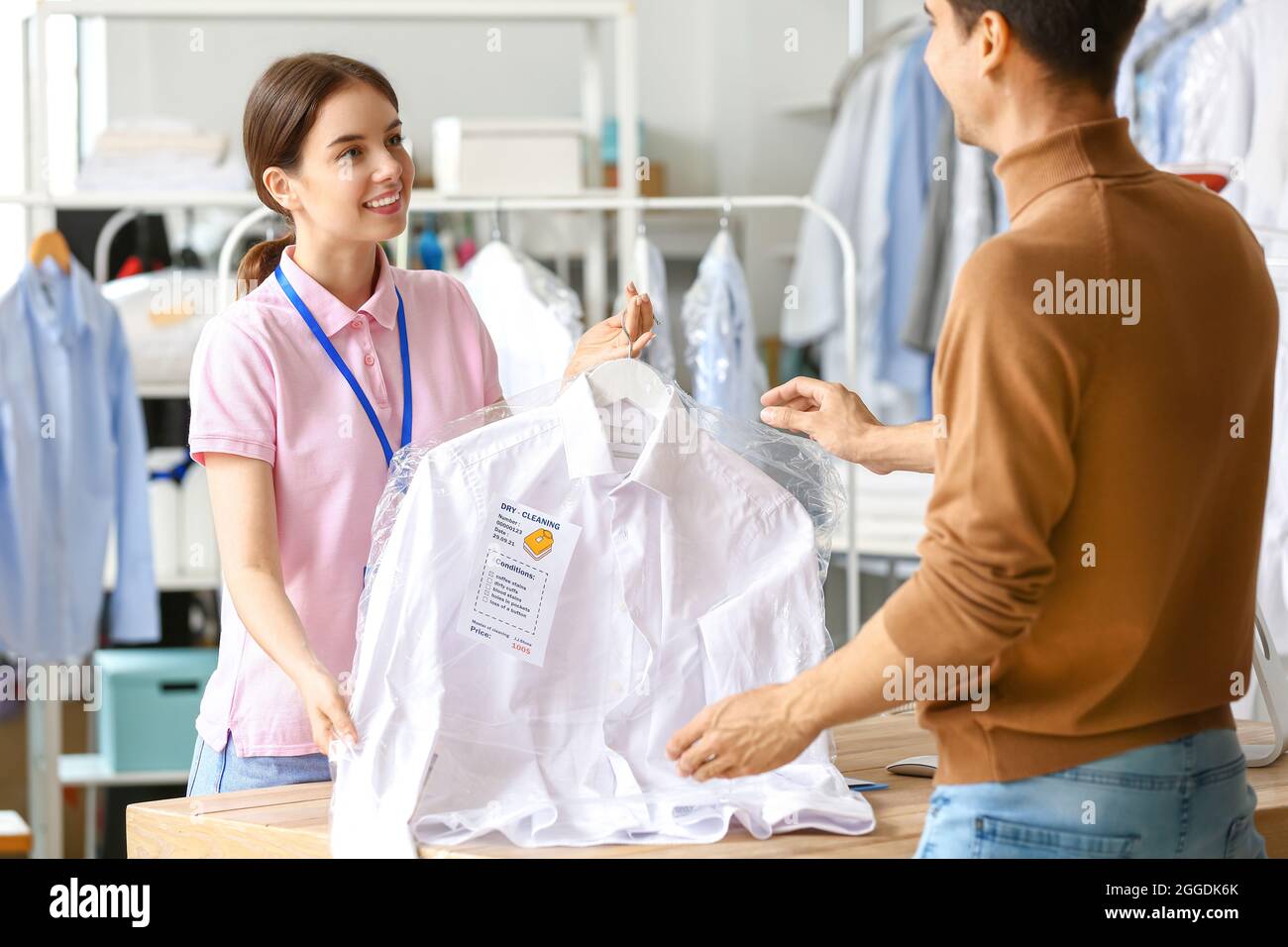 Female worker giving clean clothes to client at modern dry-cleaner's ...