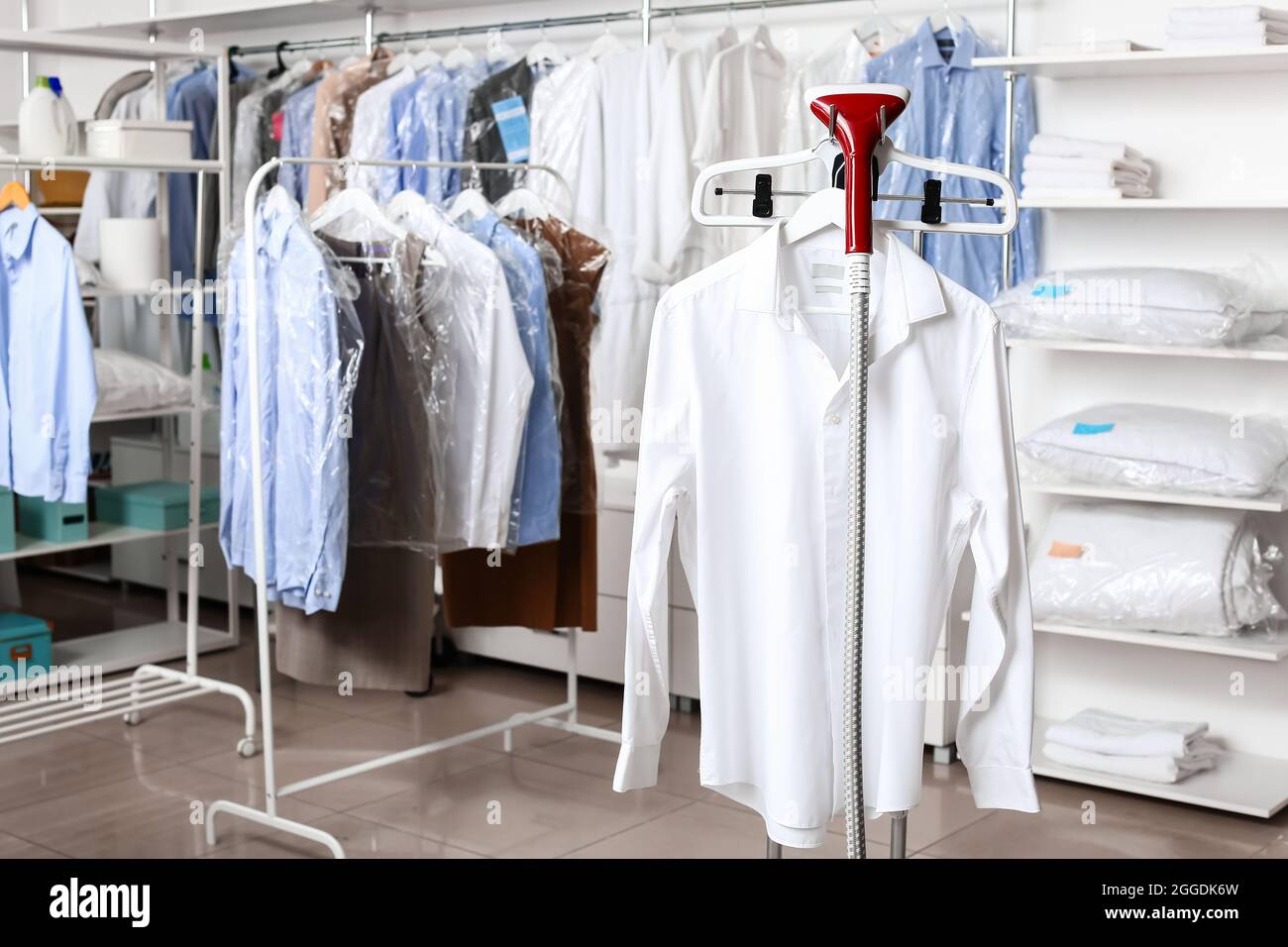 Rack with clothes and steamer in modern dry-cleaner's Stock Photo - Alamy