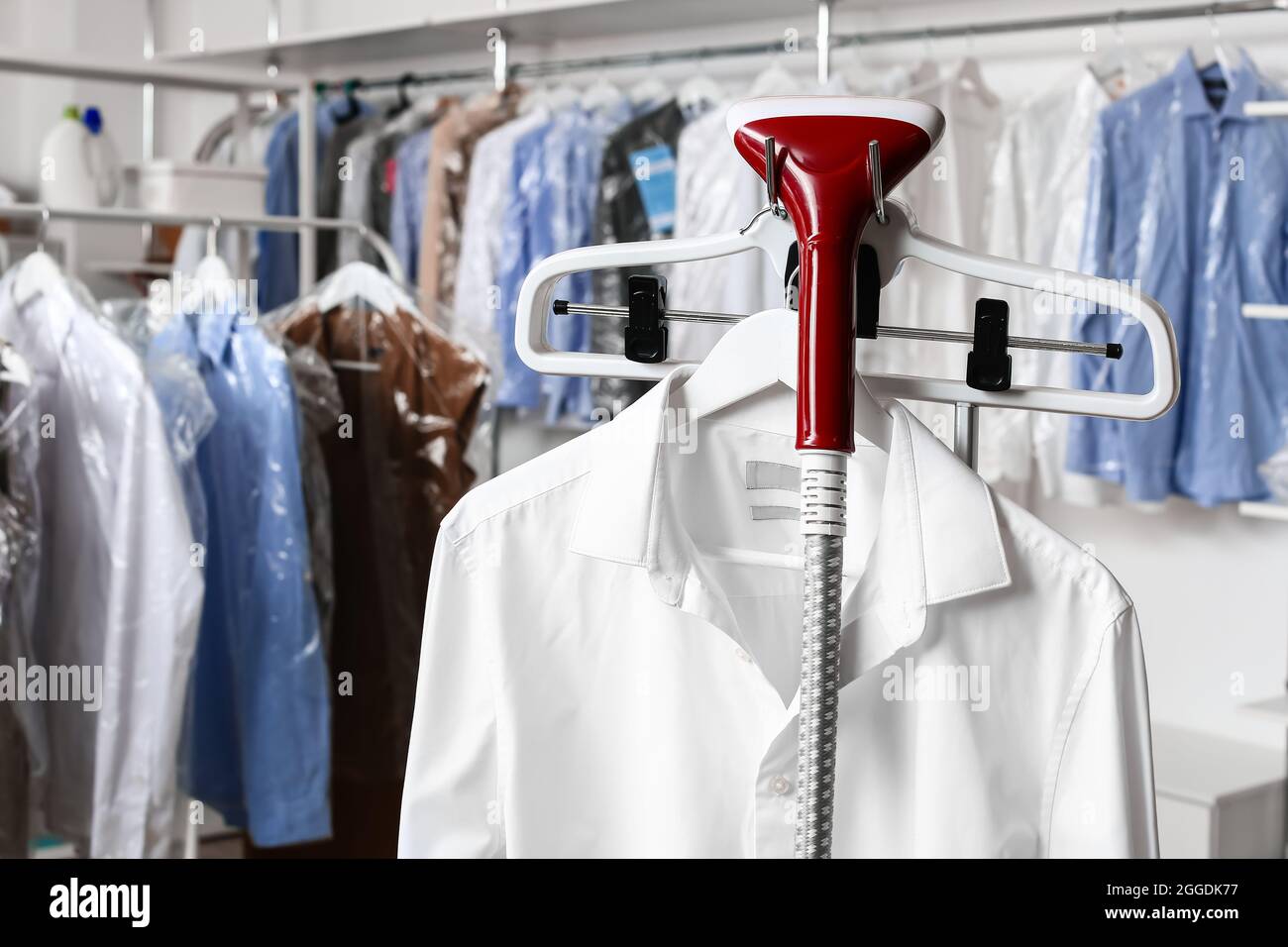 Rack with clothes and steamer in modern dry-cleaner's Stock Photo - Alamy