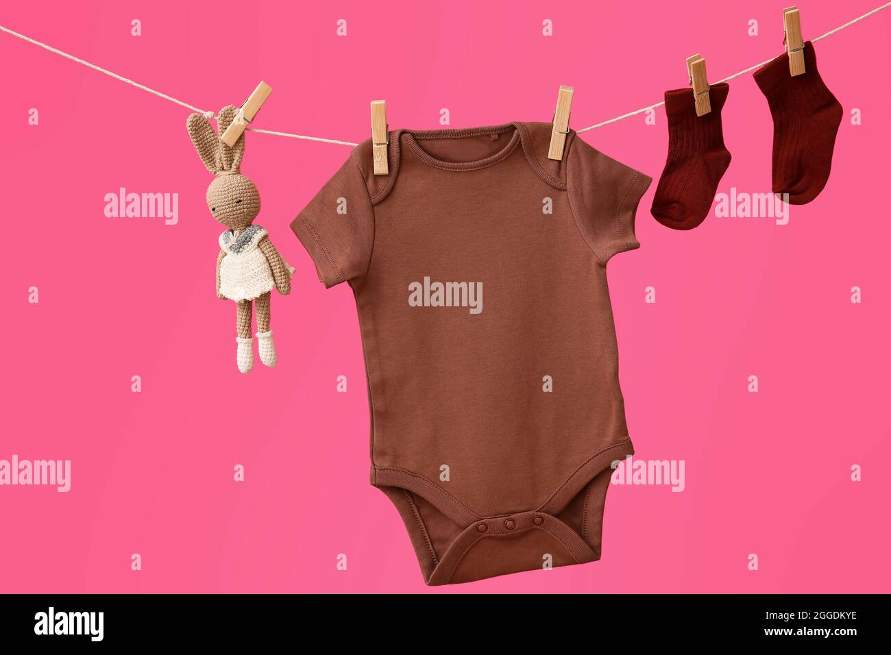 Baby clothes and toy hanging on rope against color background Stock ...