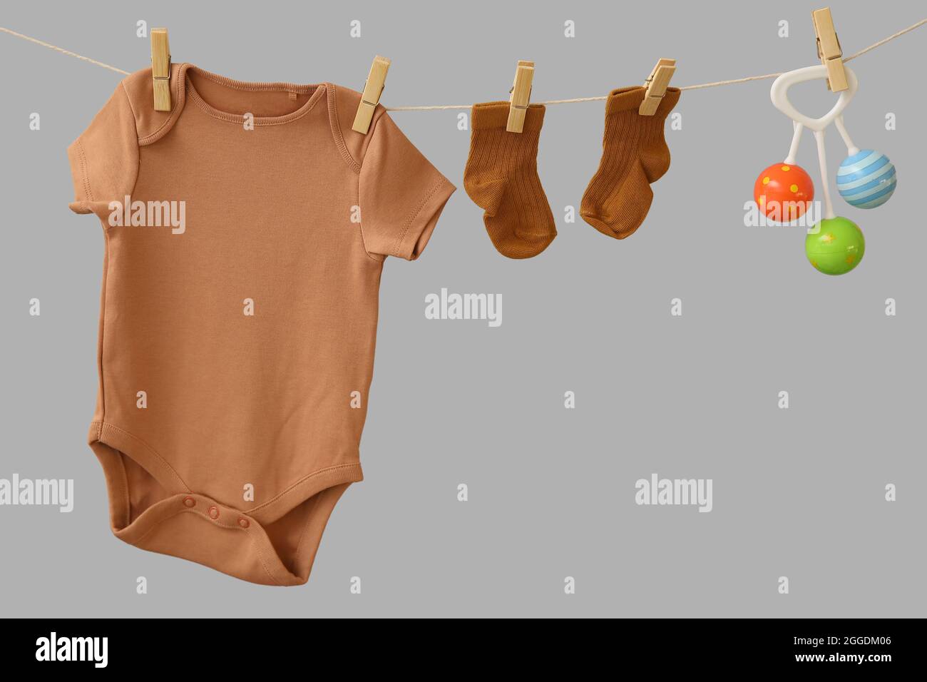 Baby clothes and toy hanging on rope against grey background Stock ...