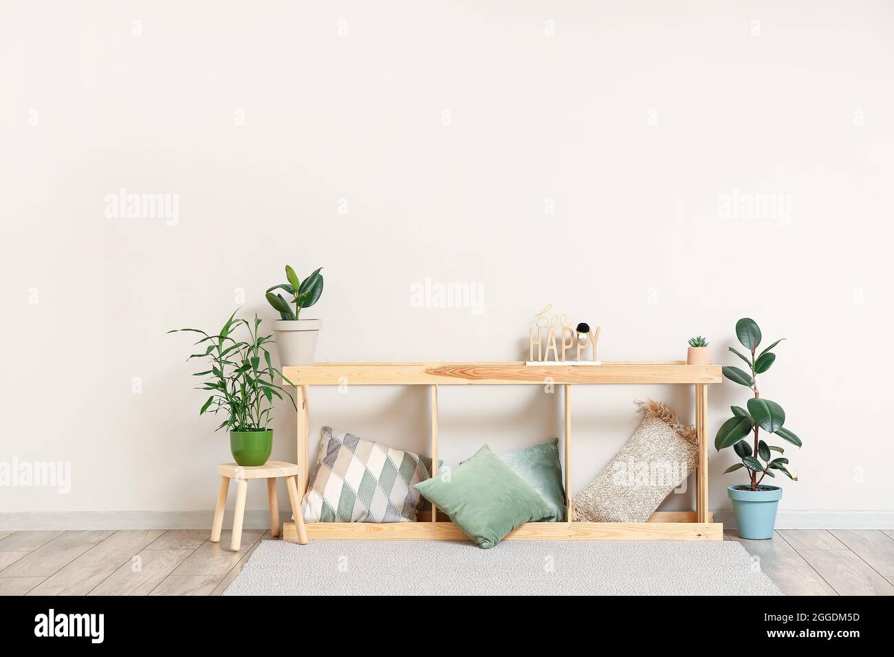 Wooden TV stand with pillows and houseplants near light wall Stock ...