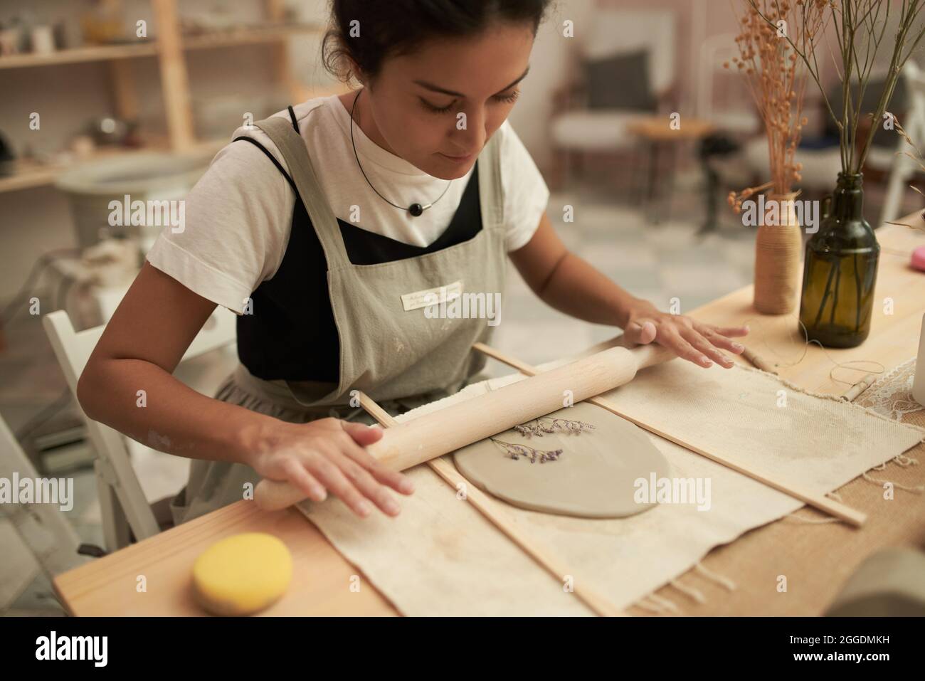 Skilled young female master pressing plants into clay piece with help ...