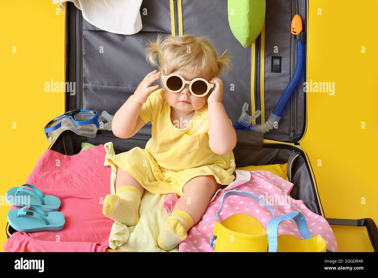 Cute baby girl in suitcase with belongings on color background Stock ...